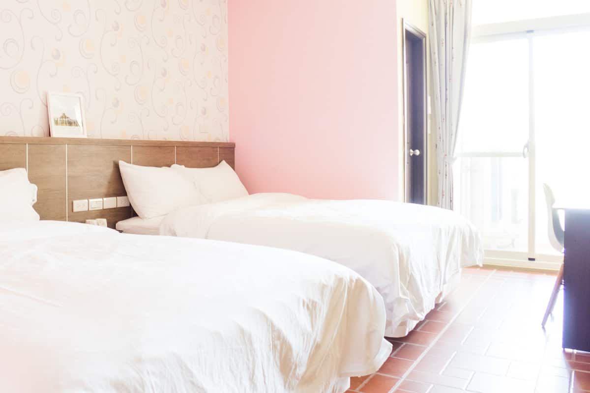 Quarto de hotel com duas camas, cabeceira de madeira, papel de parede estampado e vista para o exterior.