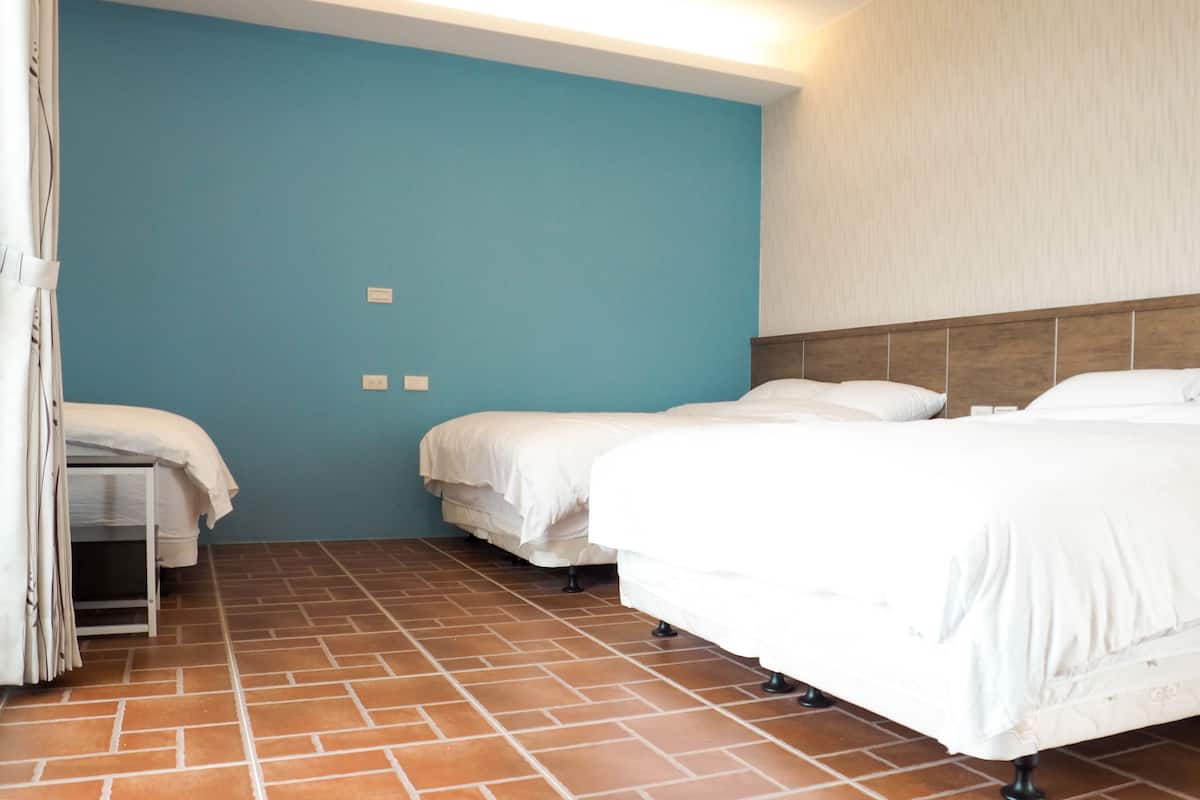 Quarto de hotel com duas camas, parede azul e chão ladrilhado.