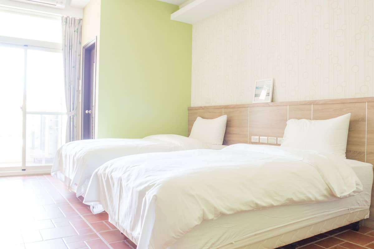 Quarto de hotel com duas camas, uma parede verde e uma janela com cortinas.