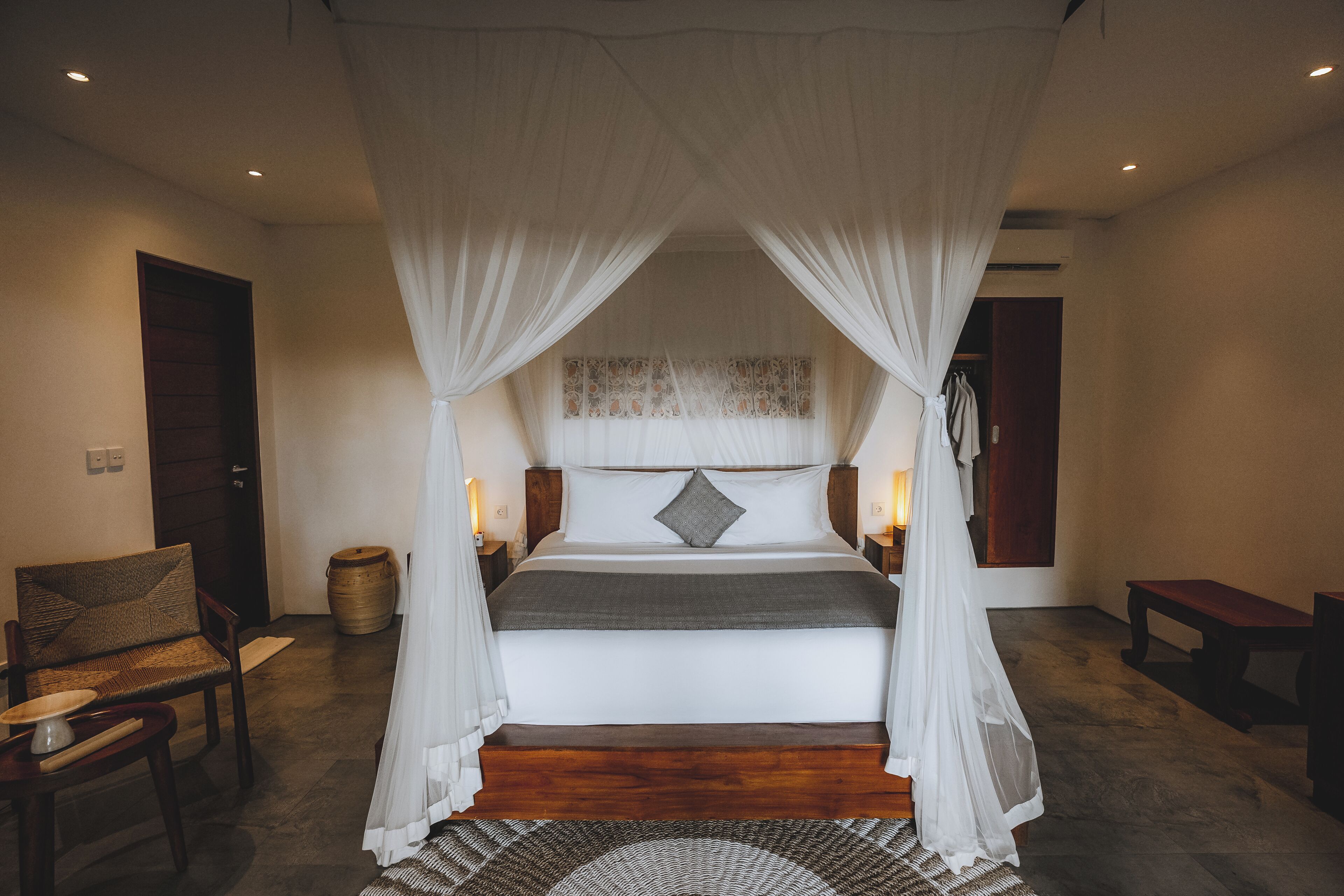 Quarto com cama de dossel, uma cadeira, mesa de cabeceira e abajur.