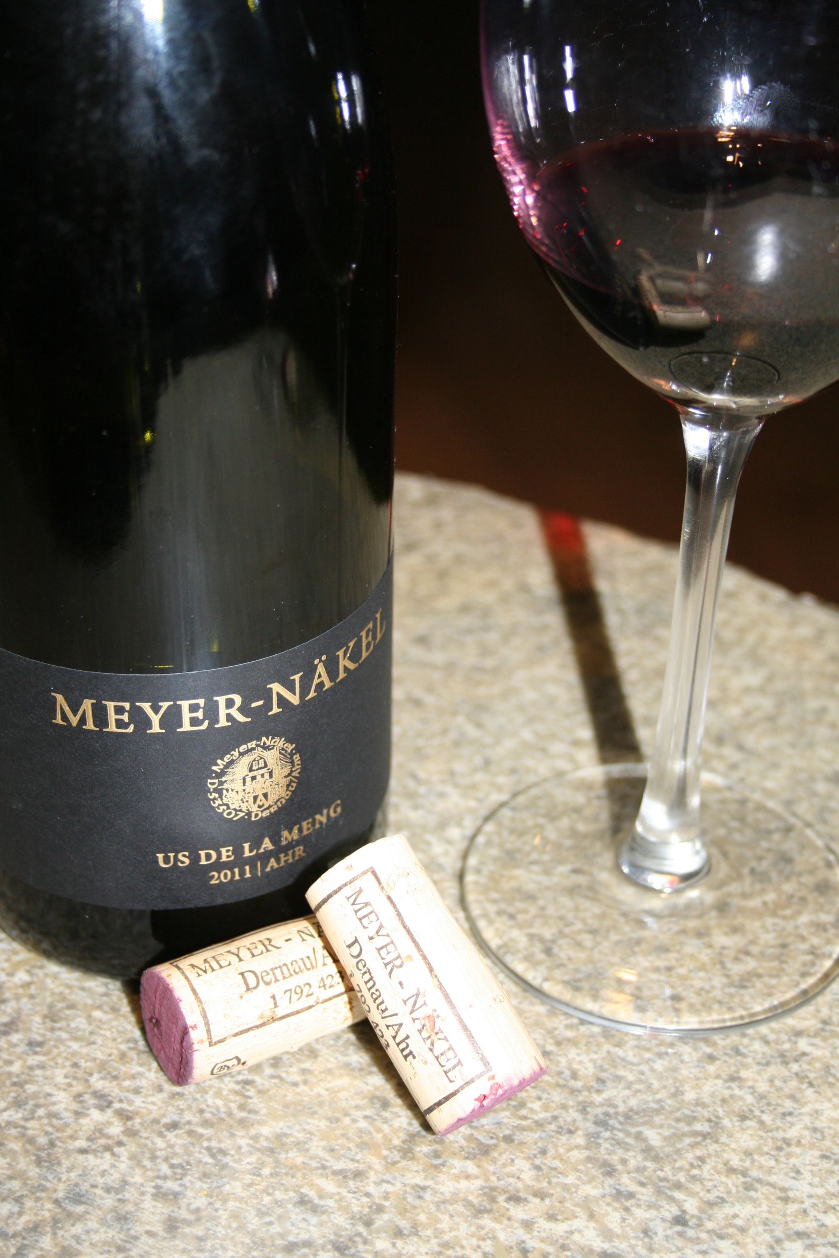 Uma garrafa de vinho Meyer-Näkel, com rolha e uma taça de vinho, sobre uma bancada.
