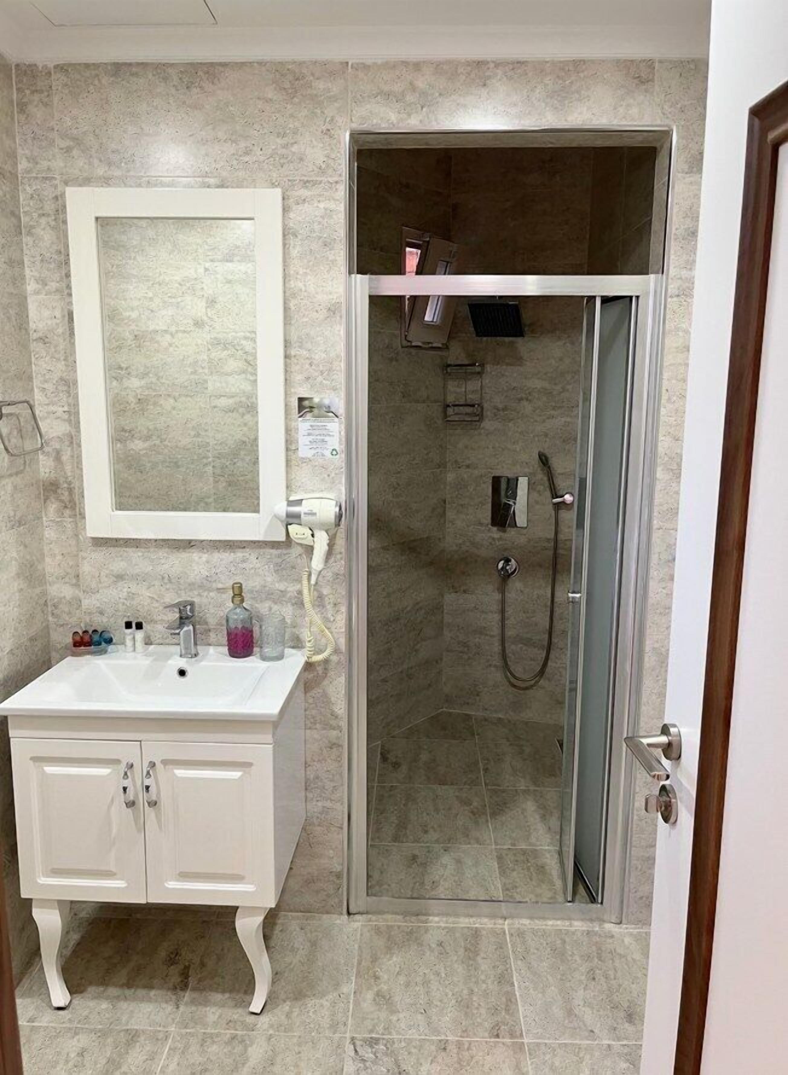 Casa de banho com toucador branco, espelho e cabine de duche.