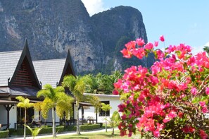Um edifício com design moderno, apresentando um telhado triangular e cercado por vegetação exuberante e flores cor-de-rosa.
