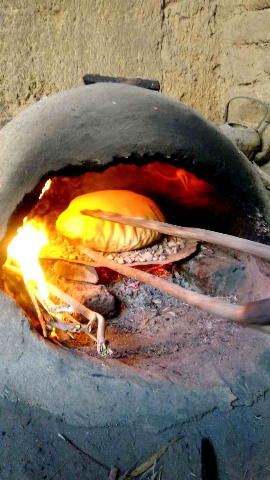 Forno tradicional com fogo aceso no interior, um utensílio de cozinha dentro e uma parede de pedra ao fundo.