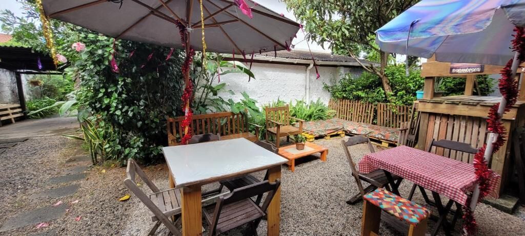 Um pátio externo com uma mesa e cadeiras, cercado por uma cerca de madeira e vegetação.