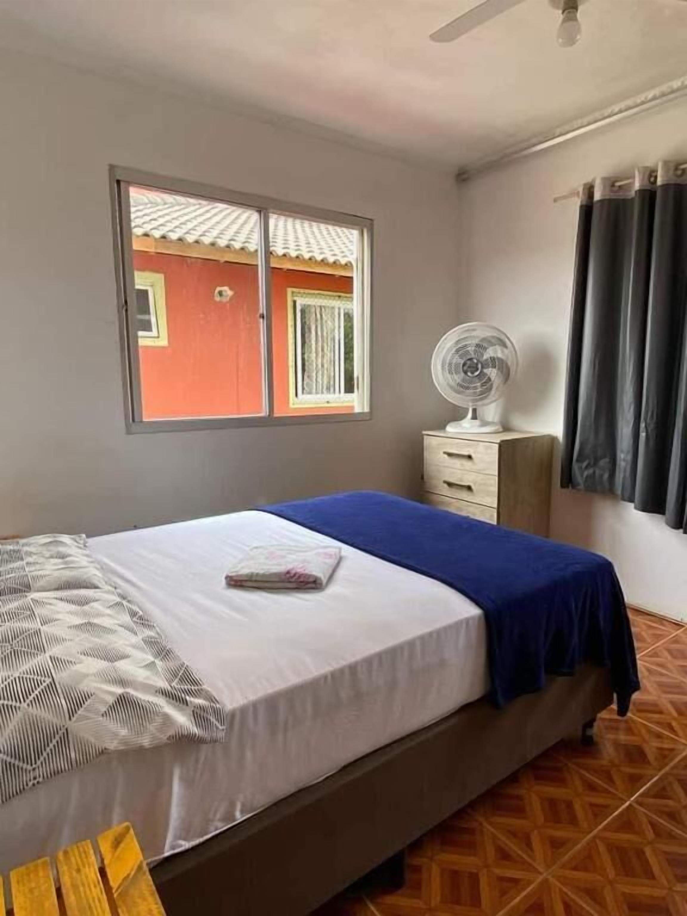 Quarto com cama, janela, ventilador e cortina.