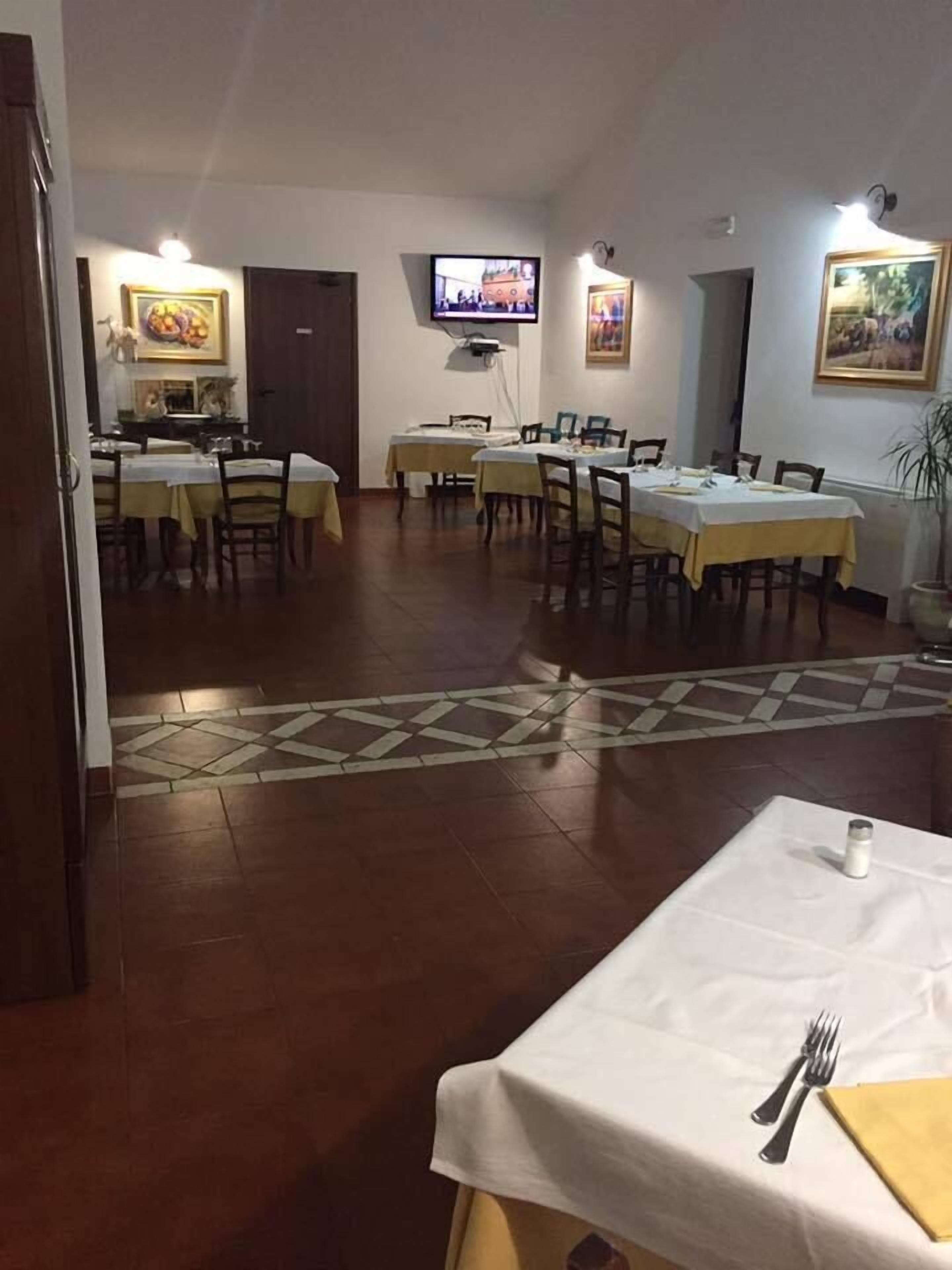 Uma sala de jantar com várias mesas e cadeiras, uma televisão presa à parede e quadros decorativos nas paredes.