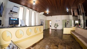 Uma área de recepção com teto de madeira, balcão de atendimento com computador e um espaço de espera com sofá.