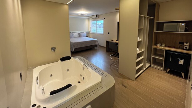Quarto moderno com cama grande, escrivaninha, cadeira, closet espaçoso e banheiro com banheira.