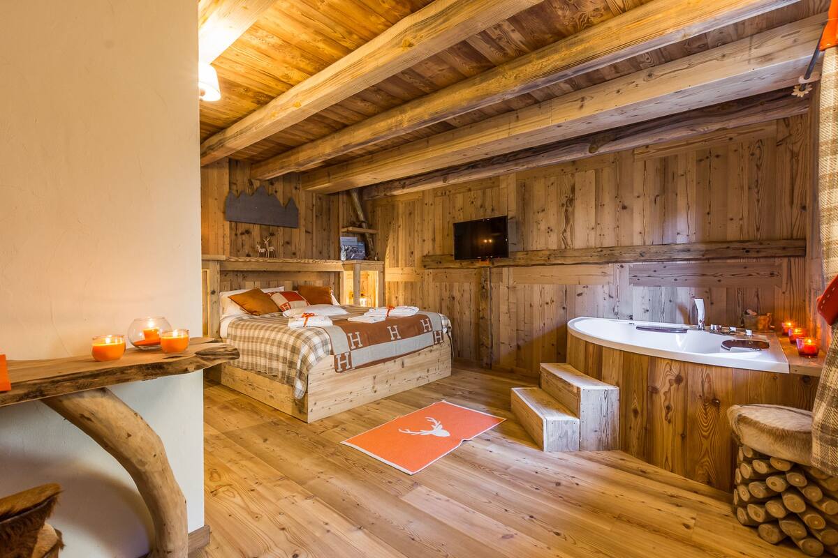 Quarto de cabana de madeira com cama, mesa de cabeceira e pequena cozinha.