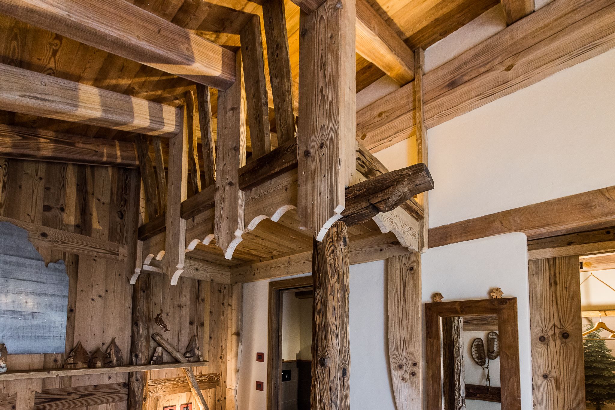 Interior rústico com vigas de madeira aparentes, uma parede branca e uma porta com um casaco pendurado.