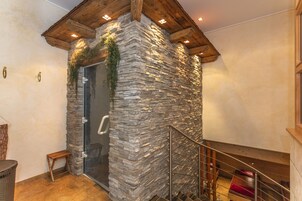 Paredes de pedra com uma porta de vidro, vigas de madeira no teto e um corrimão de metal.