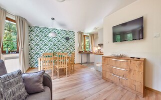 Uma sala de estar moderna com piso de madeira, um sofá, uma mesa de jantar com cadeiras, uma área de cozinha com uma TV e um papel de parede estampado.