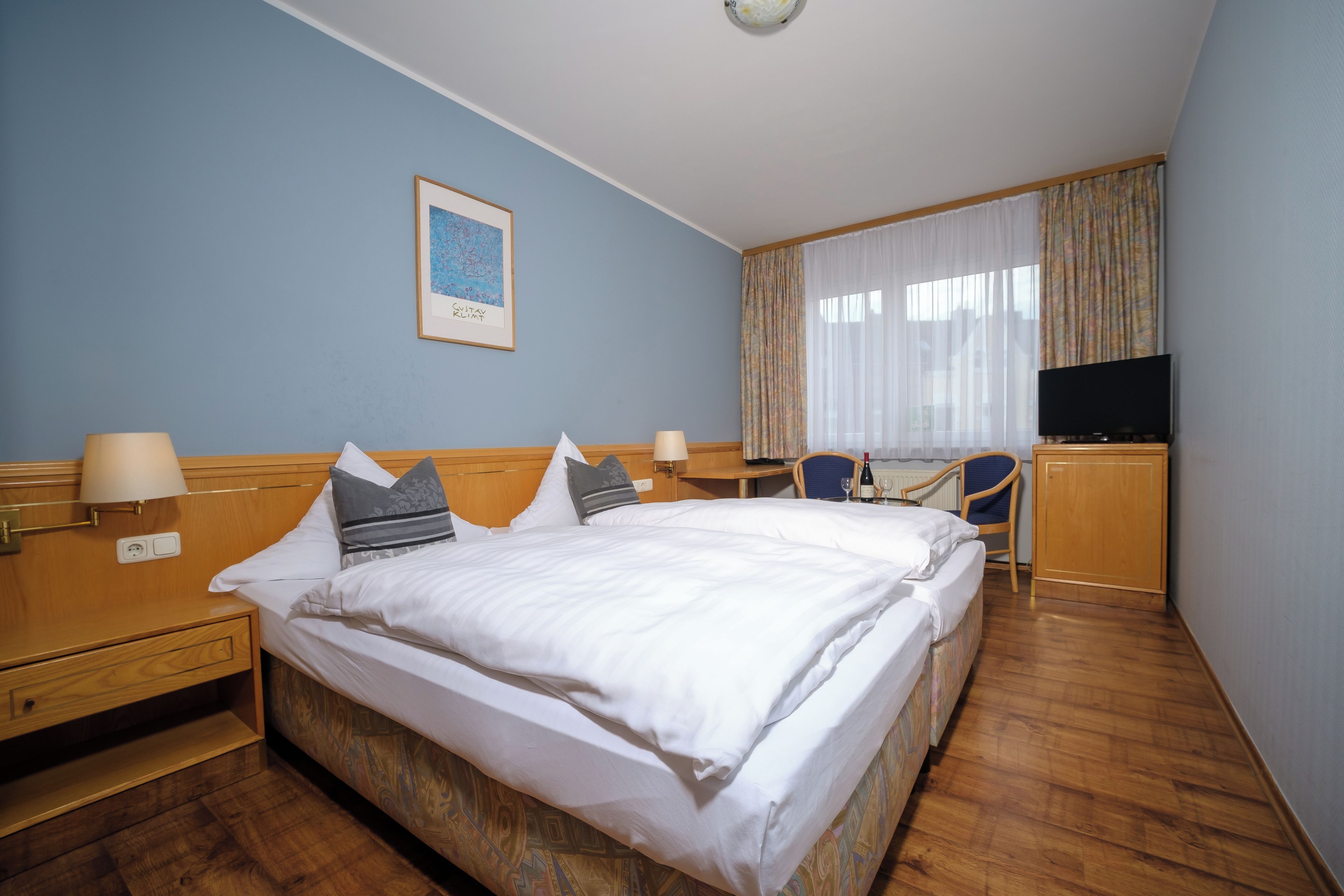 Quarto de hotel com cama grande, escrivaninha, cadeira, televisão e janela com cortinas.