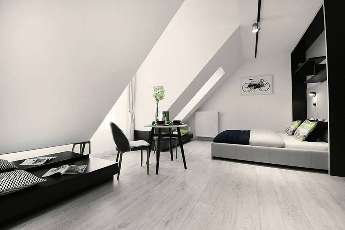 Um espaço de estar moderno estilo loft, com teto alto, área de jantar com mesa e cadeiras redondas, sofá com almofadas e uma obra de arte com tema de bicicleta na parede.