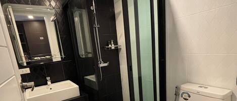 Uma casa de banho moderna com cabine de duche em vidro, sanita branca e lavatório com espelho.