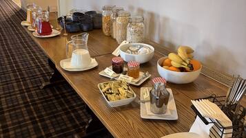 Uma mesa de buffet com diversos alimentos e acompanhamentos, incluindo potes de marmelada e uma tigela de laranjas.