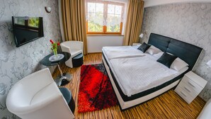 Quarto de hotel com cama, secretária, cadeira, televisão e janela com cortinas.