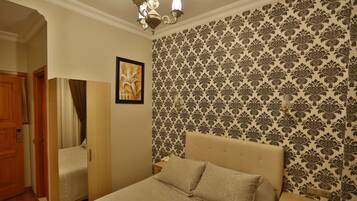 Quarto com cama, mesas de cabeceira, lustre, espelho e papel de parede estampado.