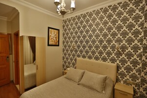 Quarto com cama, mesas de cabeceira, lustre, espelho e papel de parede estampado.