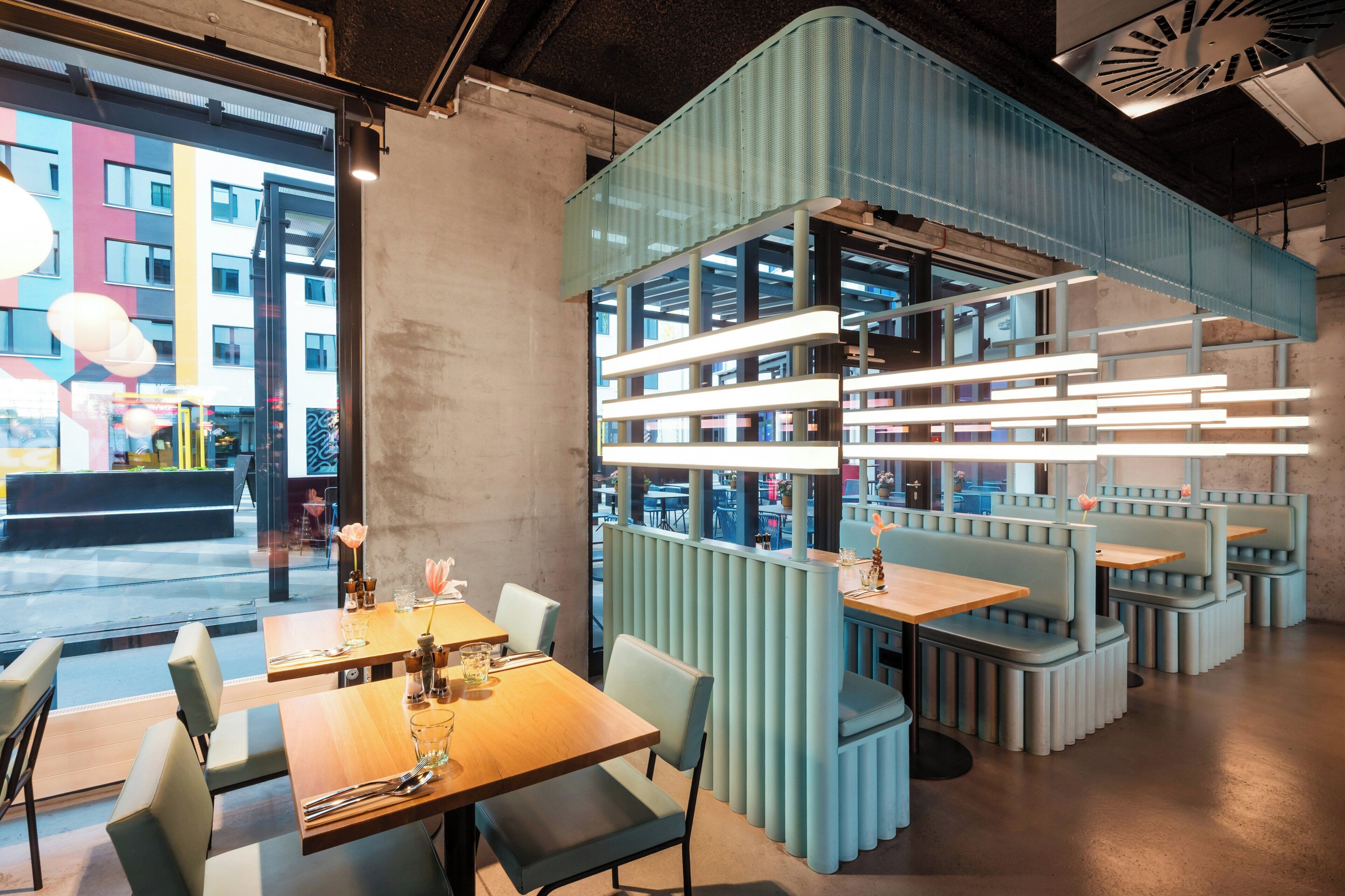 Interior moderno de restaurante com cabines, mesas e vista para um edifício colorido lá fora.