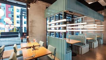 Interior moderno de restaurante com cabines, mesas e vista para um edifício colorido lá fora.