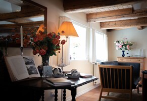 Um quarto aconchegante com uma mesa de madeira, uma luminária, uma cadeira e um vaso com flores.