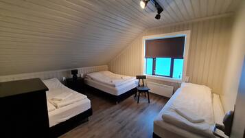 Um quarto de sótão pequeno e acolhedor, com duas camas, um aquecedor e uma janela com persianas.