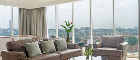 Uma sala de estar moderna com um sofá de couro marrom, uma mesa de centro redonda e uma janela grande com vista para a cidade.