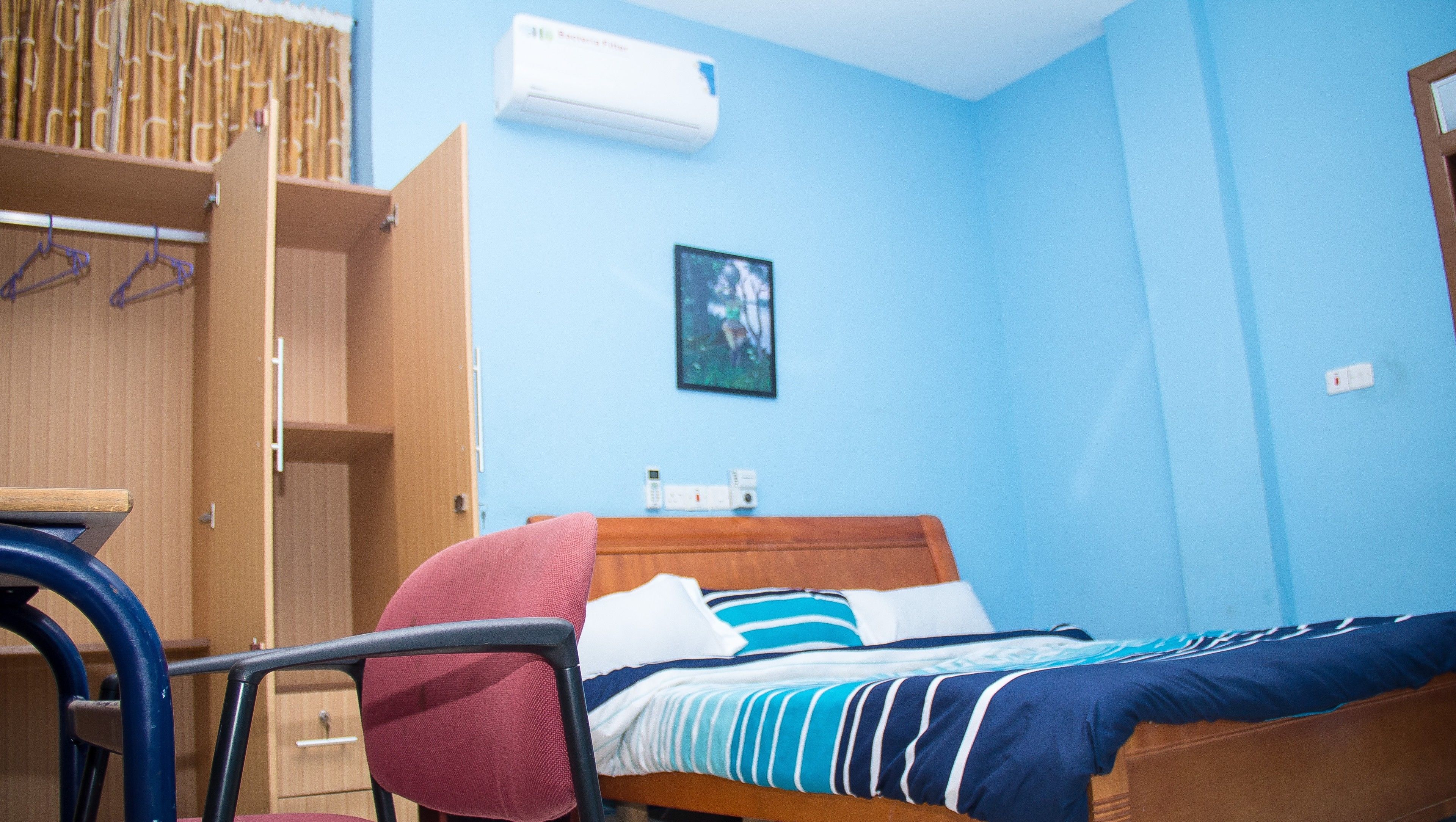 Quarto com cama, guarda-roupa de madeira, uma cadeira e ar condicionado fixado na parede.