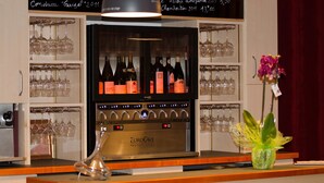 Uma área de bar com um dosador de vinho, copos de vinho e um vaso com flores.
