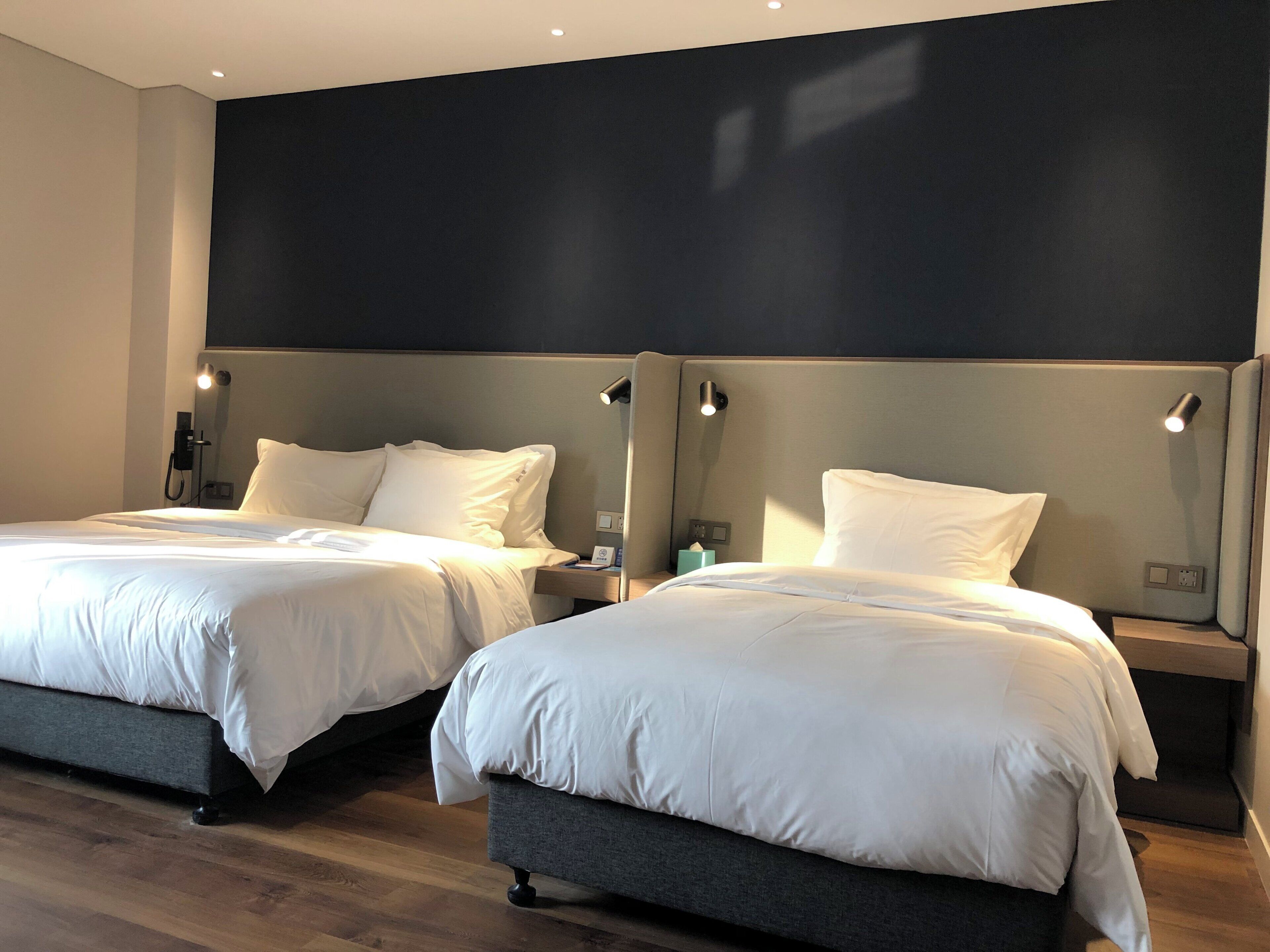 Quarto de hotel com duas camas, cada uma com mesa de cabeceira, luminária e telefone.