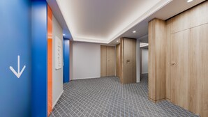 Um corredor com uma seta indicativa na parede, piso de azulejos e portas de madeira.