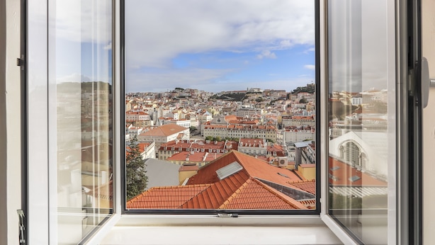 Vista urbana através de uma janela, com prédios e uma colina ao longe.
