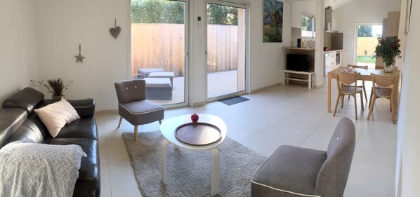 Uma sala de estar moderna com sofá, mesa de centro e área de jantar com cadeiras e televisão.