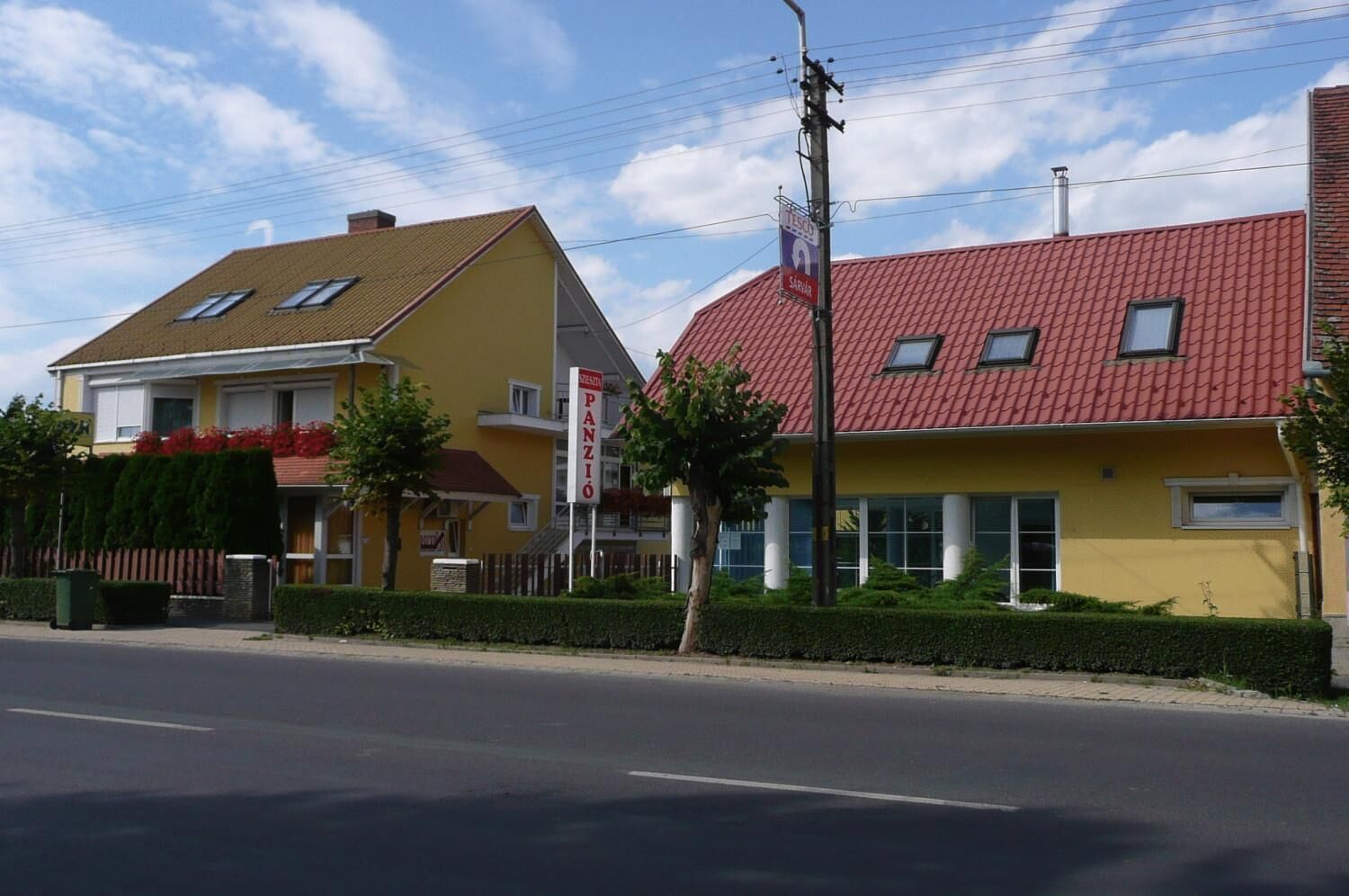Um edifício amarelo com telhado vermelho, uma placa de identificação visível e uma estrada desimpedida na frente.