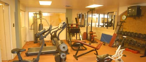 Uma academia com máquinas de cardio, equipamentos de musculação e um espelho na parede.
