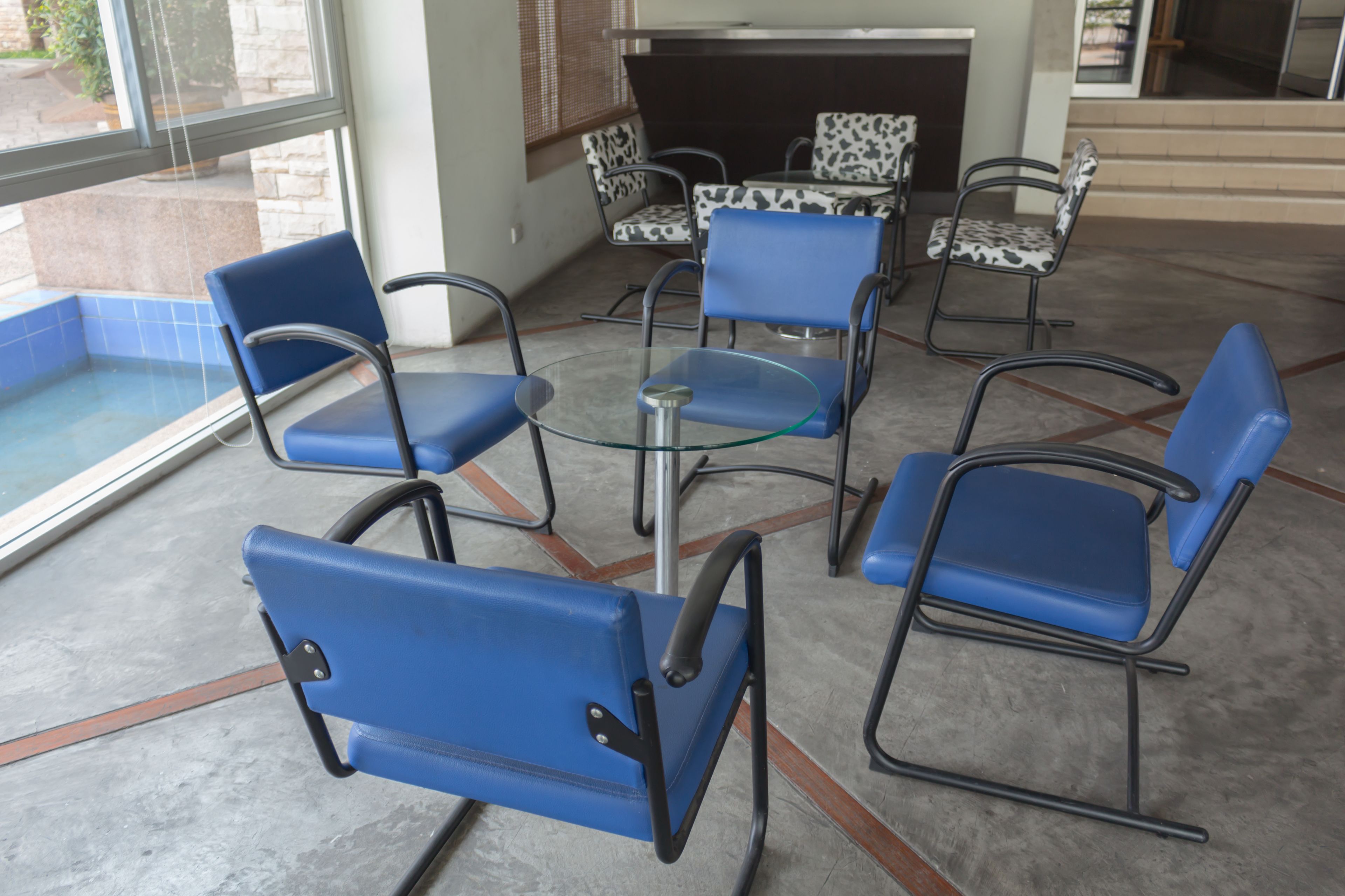 Uma área de estar com cadeiras azuis, uma mesa de vidro, lareira e vista para uma piscina através de uma janela.