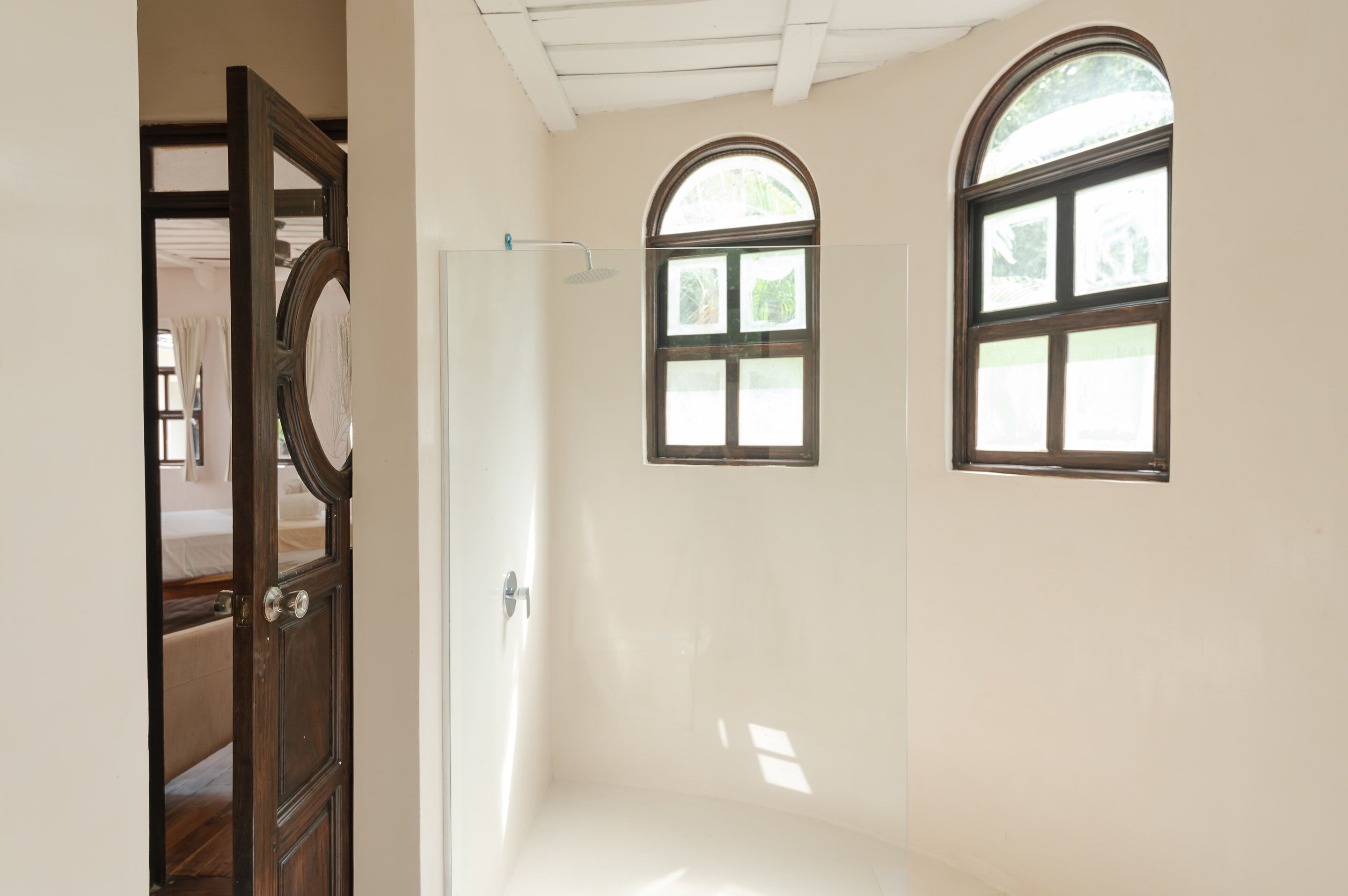 Um quarto com uma grande janela em arco, uma porta com espelho e área de chuveiro.