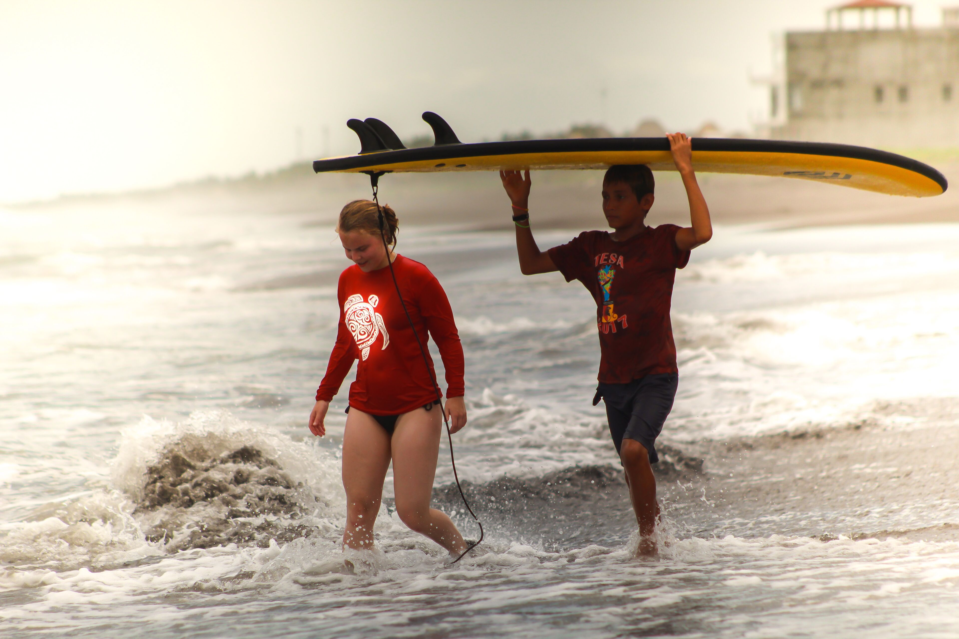 Duas pessoas carregando uma prancha de surf na água.