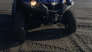 Um veículo todo-terreno azul estacionado numa praia de areia, com o oceano ao fundo.