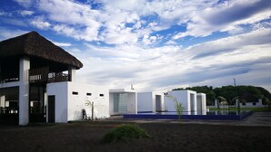 Um edifício moderno com estrutura de telhado de palha, paredes brancas e área de piscina.