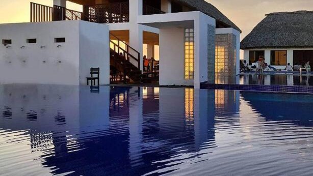 Um resort com piscina, um edifício com telhado de palha e uma construção branca com varanda.