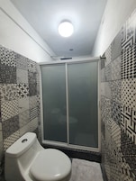 Um banheiro com vaso sanitário, chuveiro com porta de vidro e azulejos estampados nas paredes.