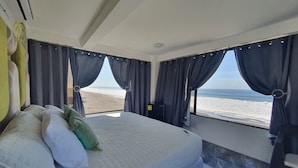 Quarto com cama, mesa de cabeceira e vista para a praia.
