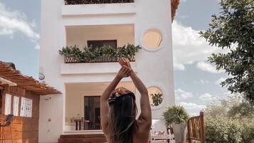 Uma pessoa sentada à beira da piscina, em frente a um edifício com varandas e janelas circulares.