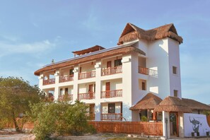 Um hotel com vários andares, varandas com telhados de palha e fachada branca.