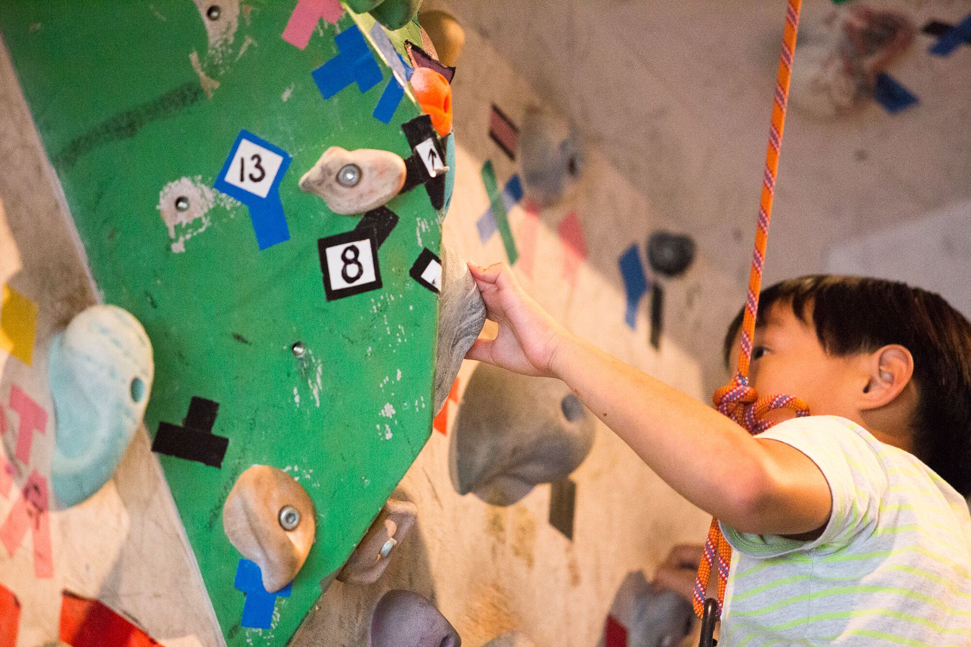 Criança escalando uma parede de escalada com apoios numerados.