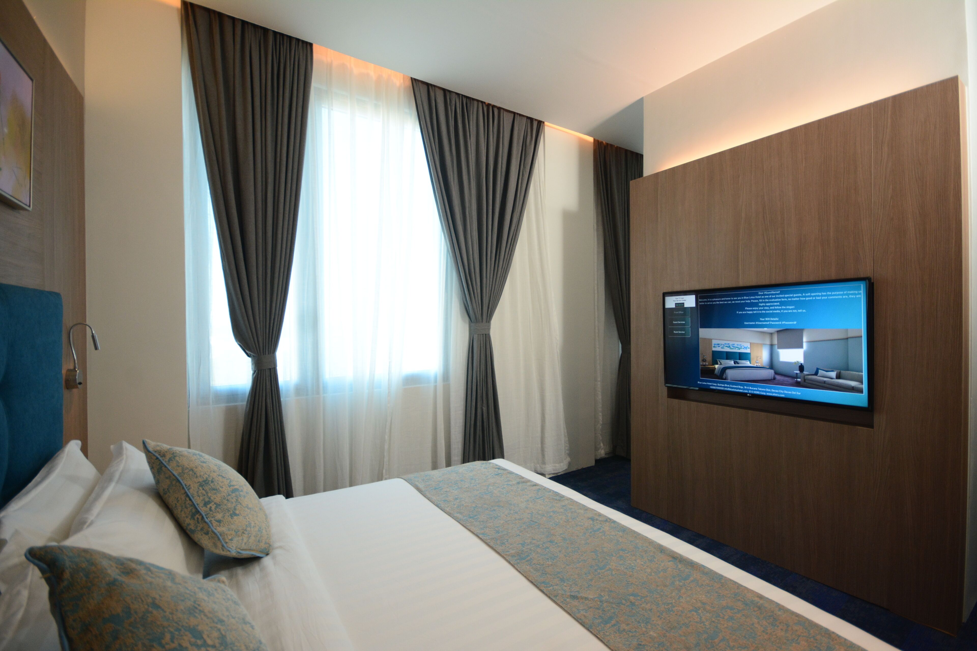 Quarto de hotel com cama, cortinas, televisão e parede revestida de madeira.