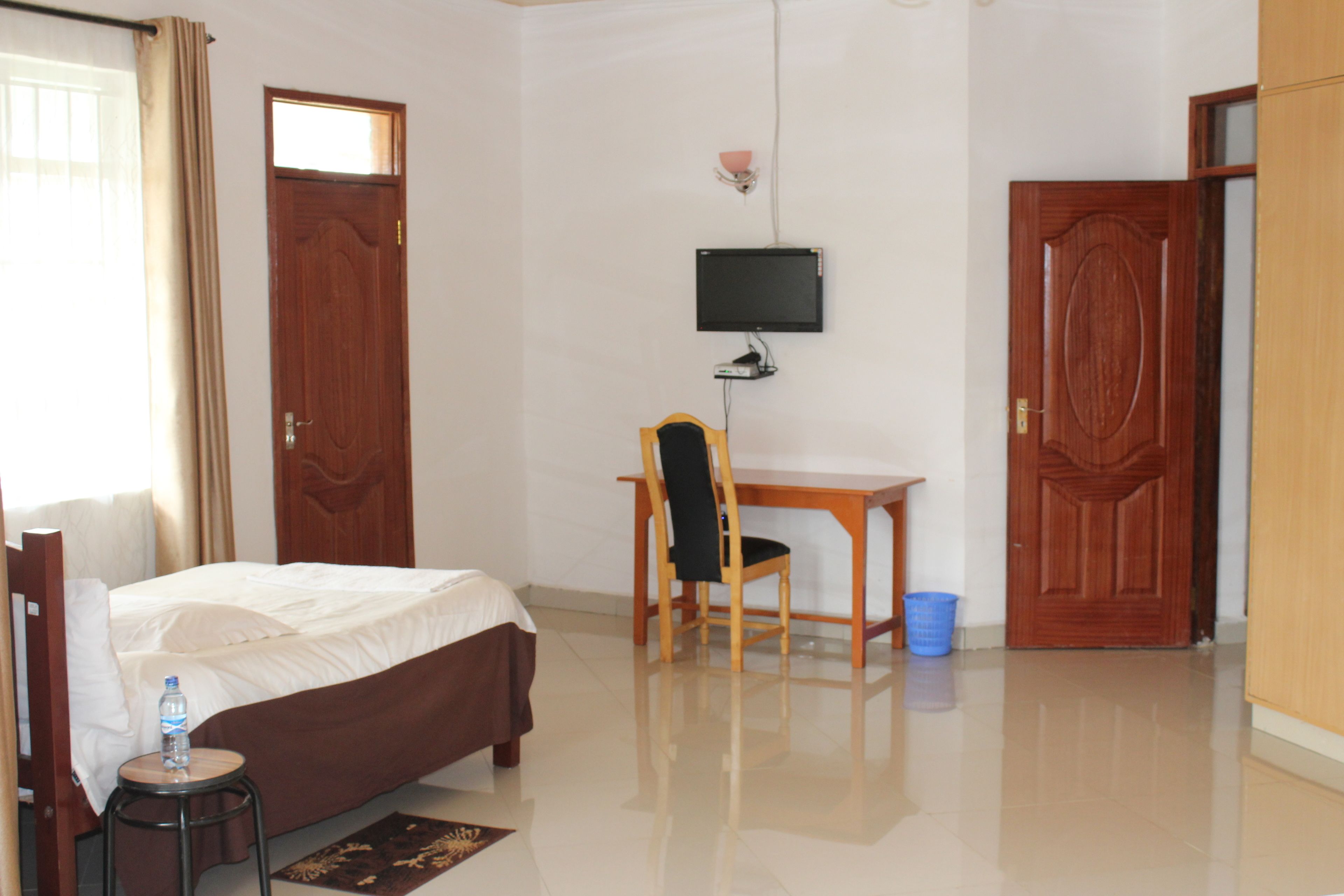Quarto com cama, escrivaninha, cadeira, televisão e porta.